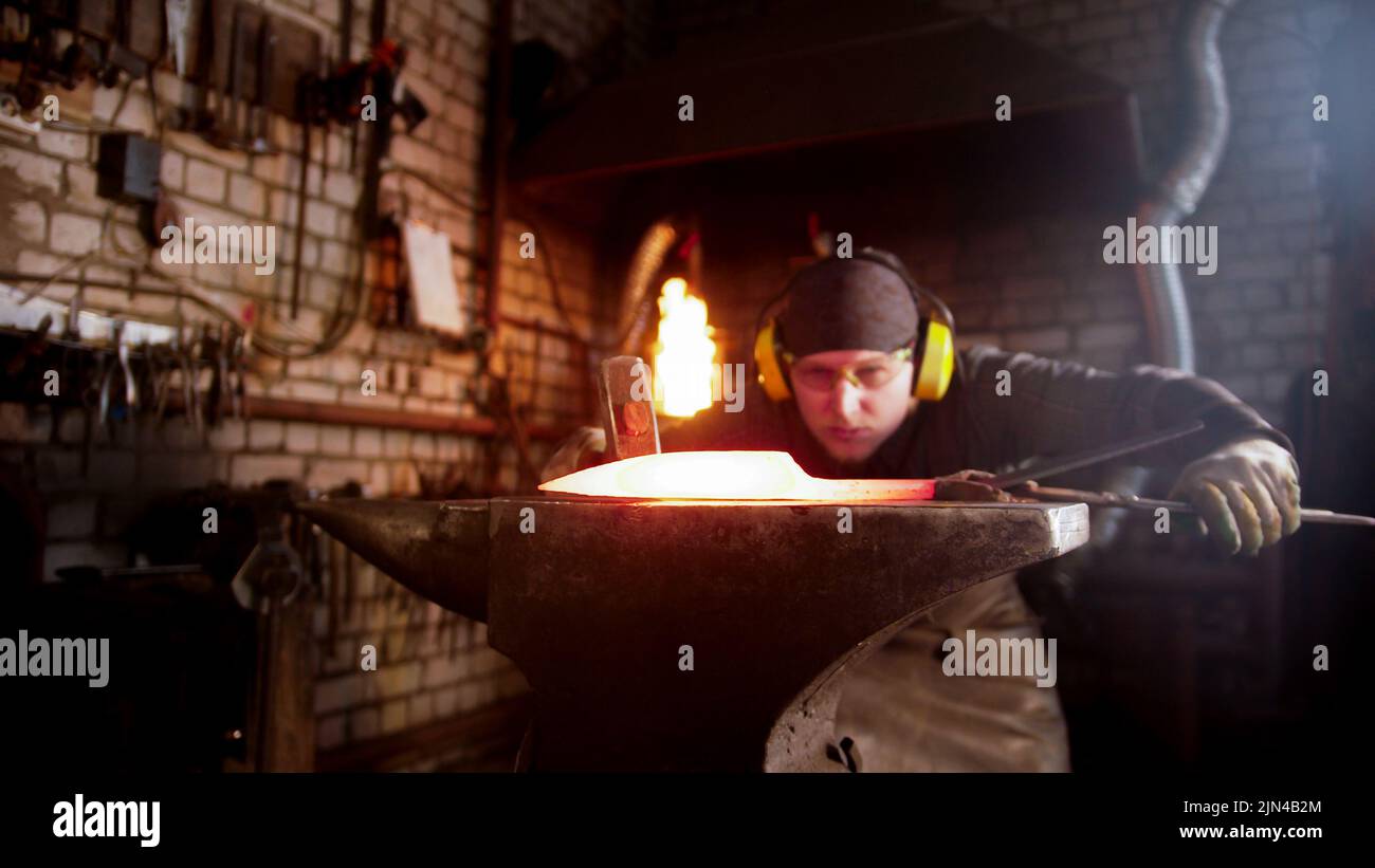 Blacksmith forging a knife blade in workshop using a hammer Stock Photo ...
