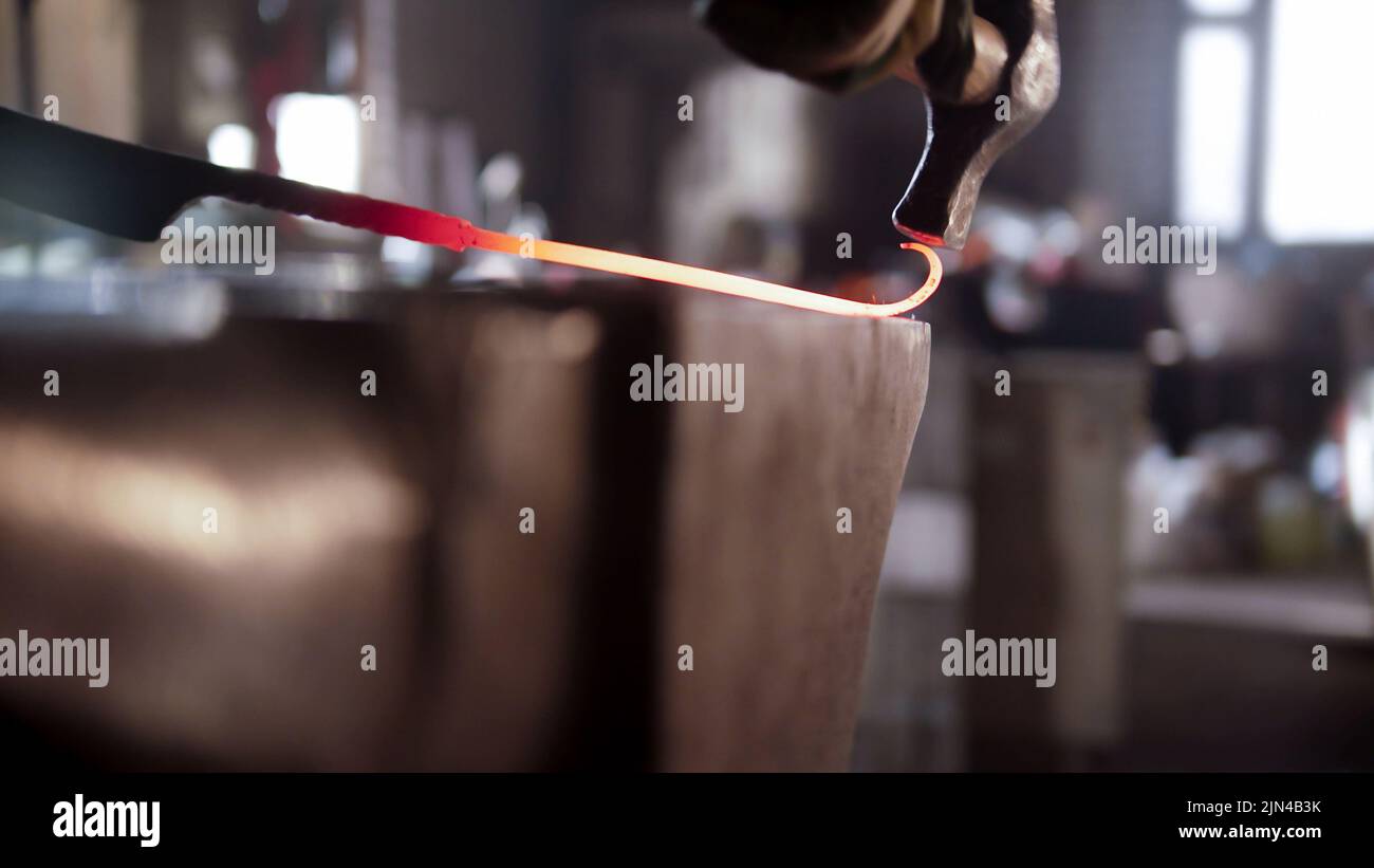 Blacksmith torque the longer piece of metal in a spiral using a hammer ...