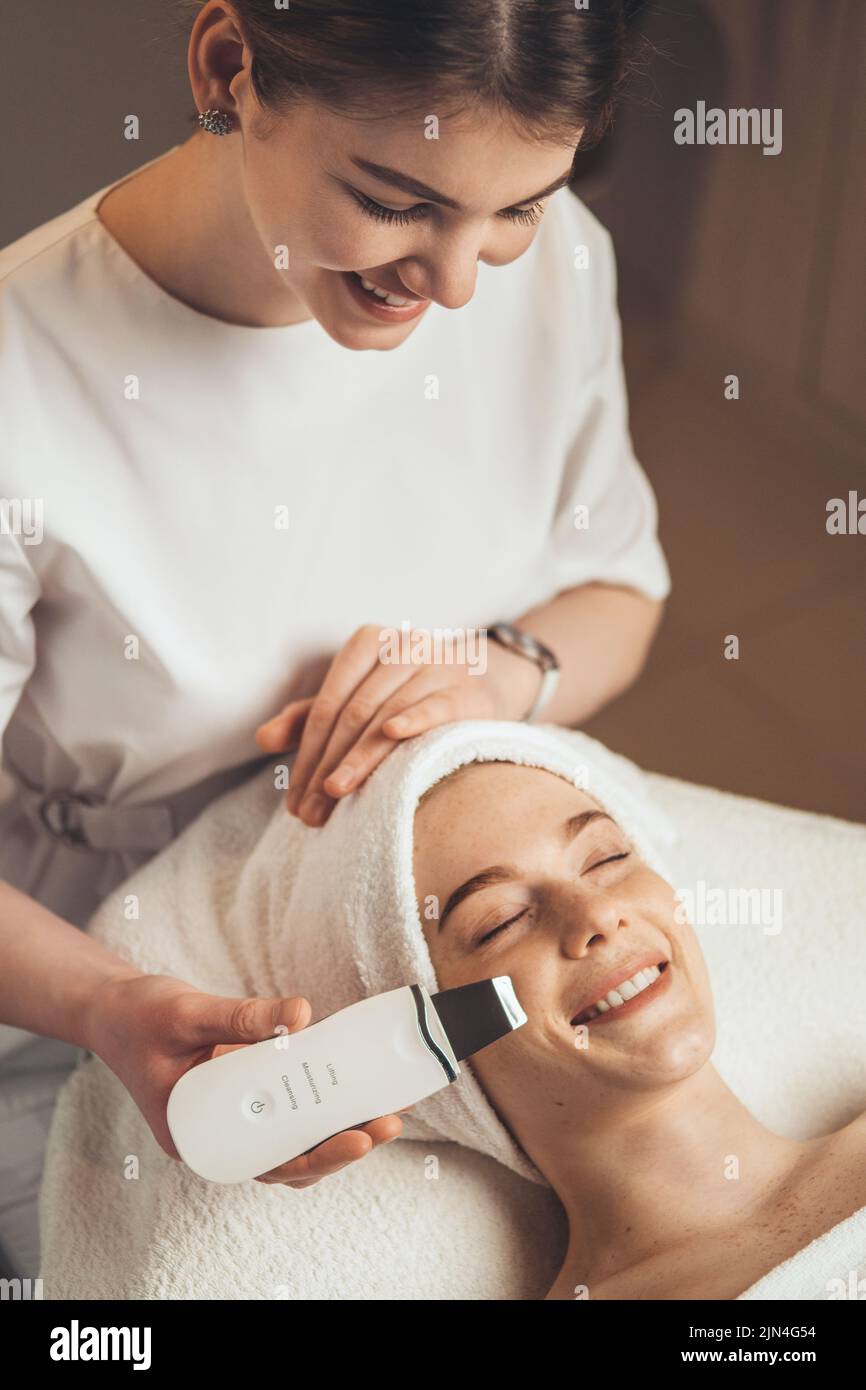 Beautician with ultrasonic scrubber cleansing woman's face skin at spa ...