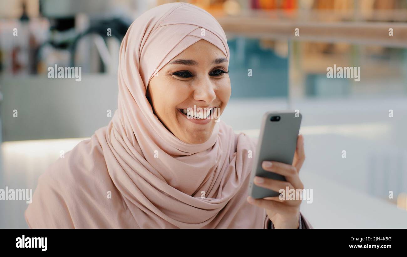 Happy young muslim woman in hijab holding smartphone playing on phone ...