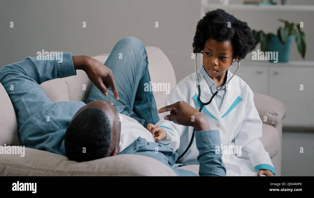 Cute little girl in medical gown plays with dad pretending to be doctor ...