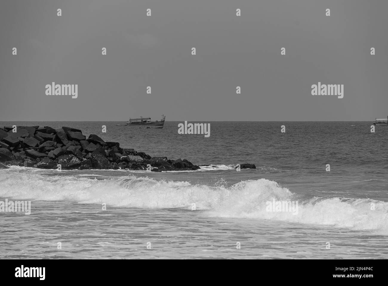 An aerial view of sea waves near rocks in background of floating boat ...