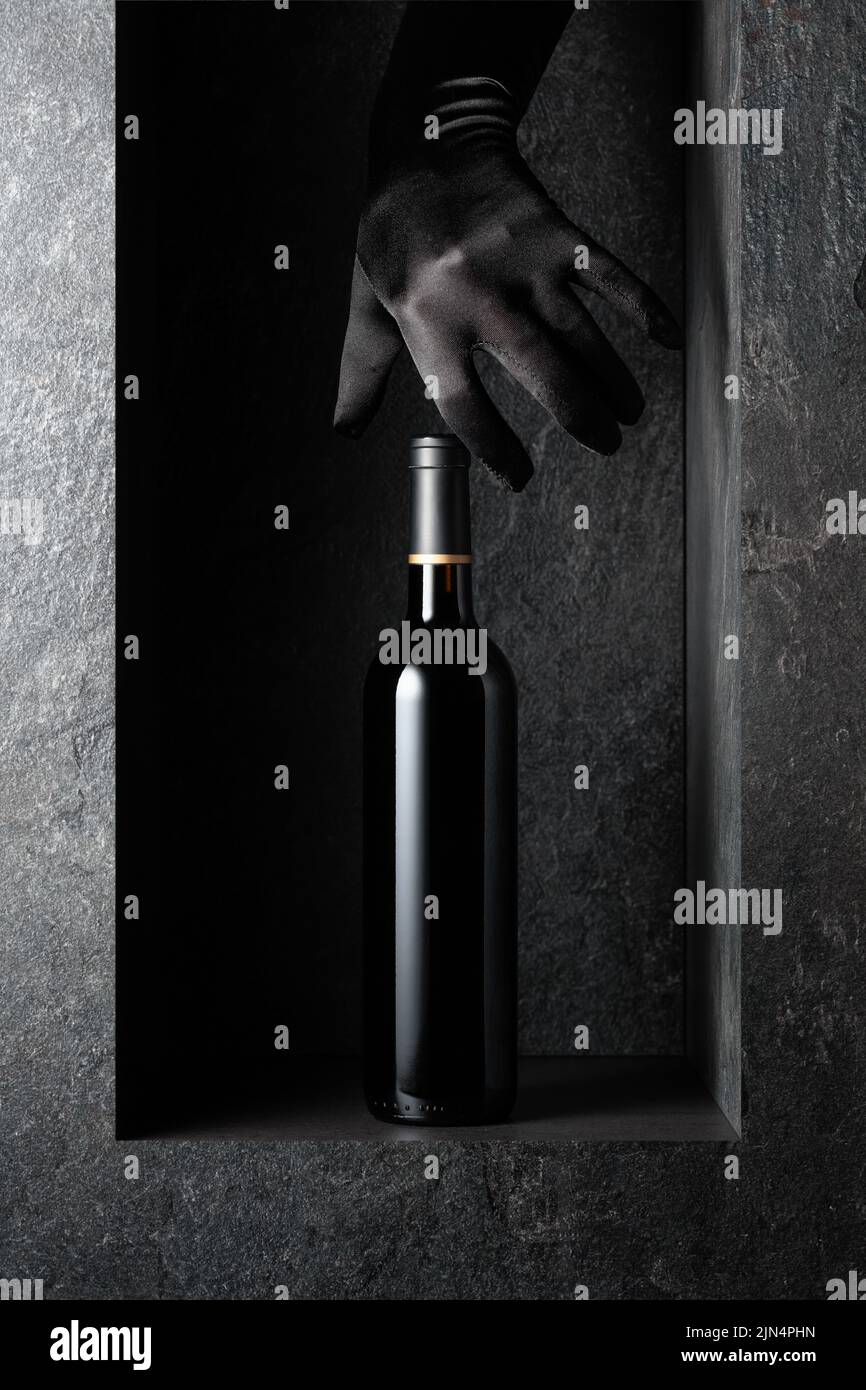A woman's hand in a black glove reaches for a bottle of red wine. A ...