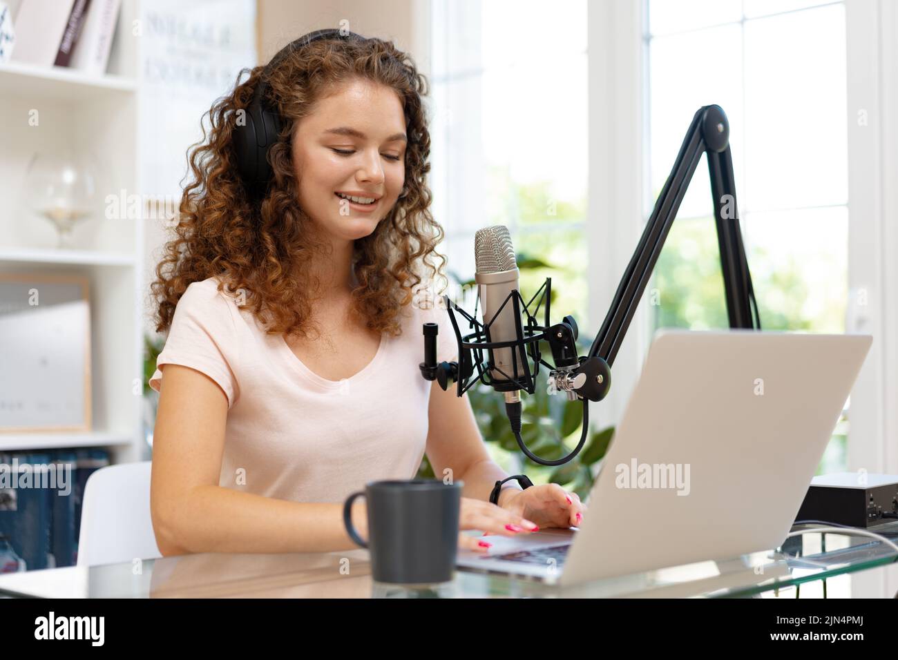 Young curly female recording podcast from home and talking into a ...