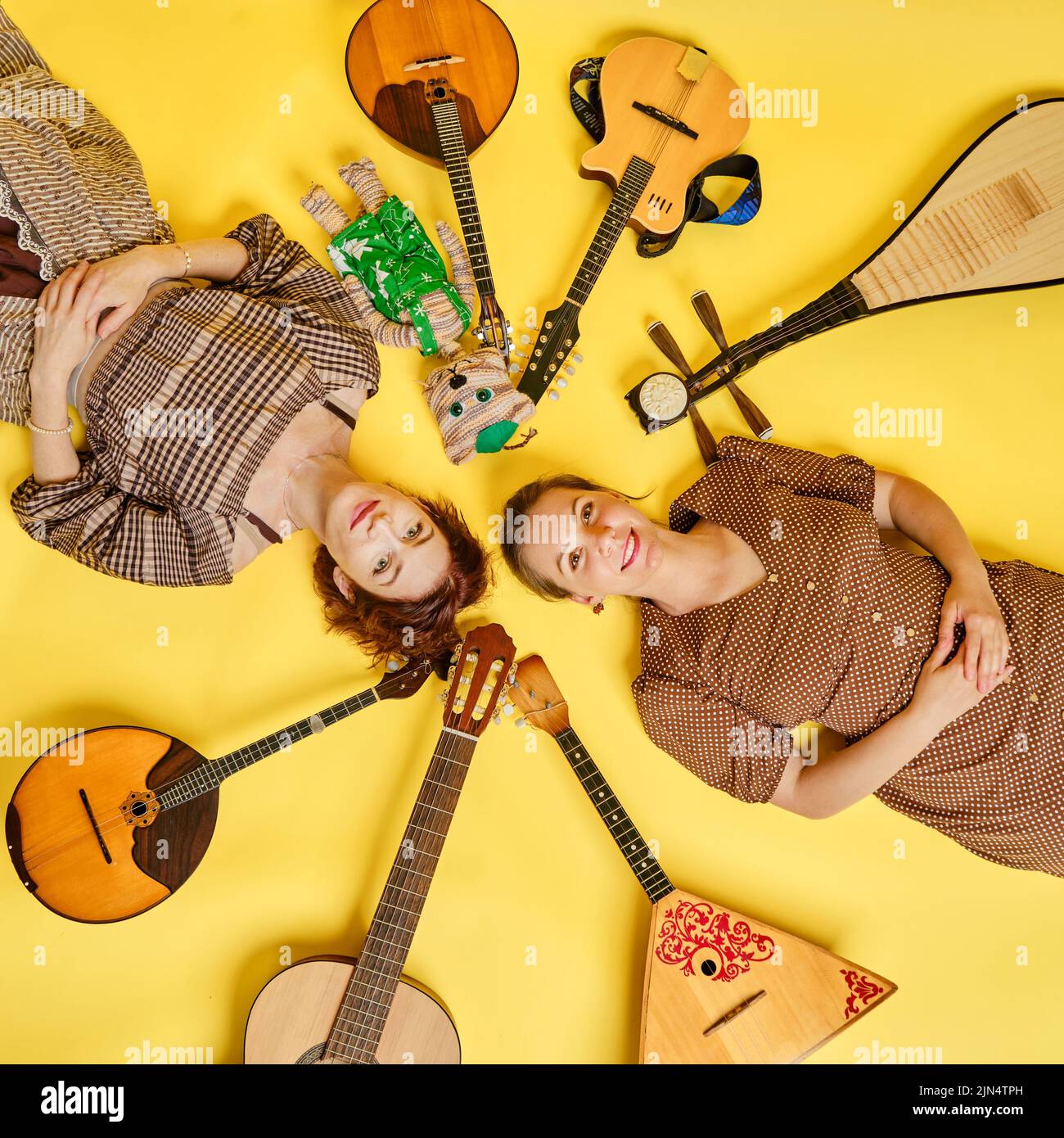 Women musicians in dresses with musical instruments on a yellow studio ...