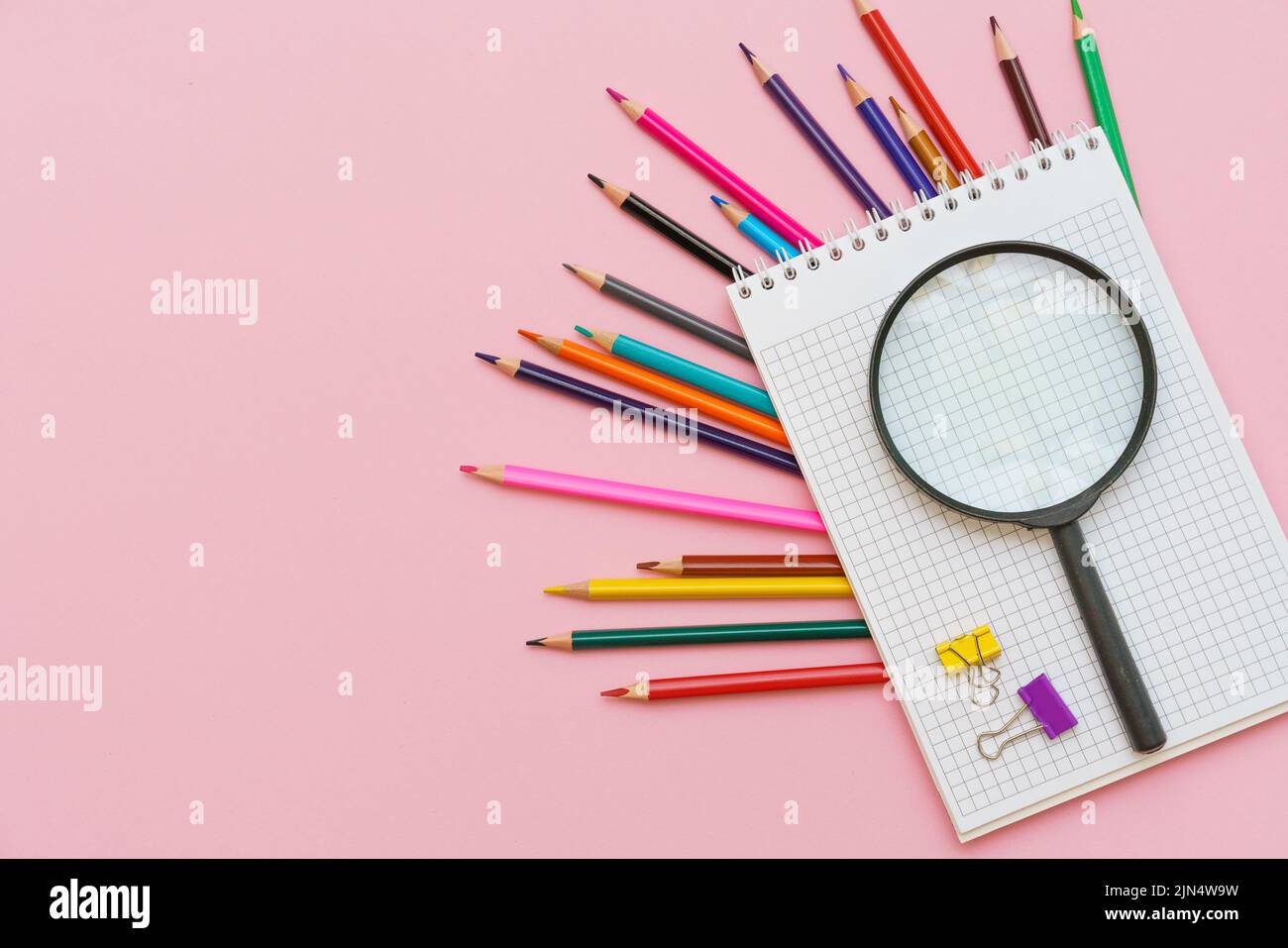 Magnifying glass, pencils and a blank white notepad on a spring on a ...
