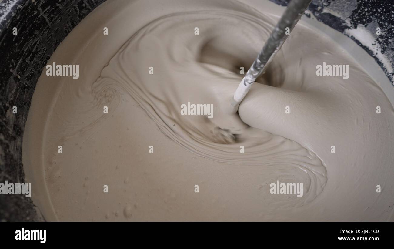 A worker using a mixer mixes the self-leveling floor in a bucket. Stir ...