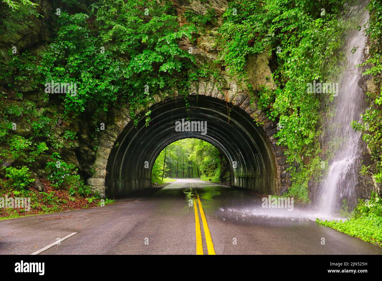 A tunnel through a mountain with a waterfall flowing down in front of ...