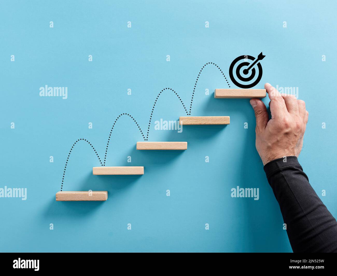 Male hand arranges a wooden block staircase with target icon. Achieving ...