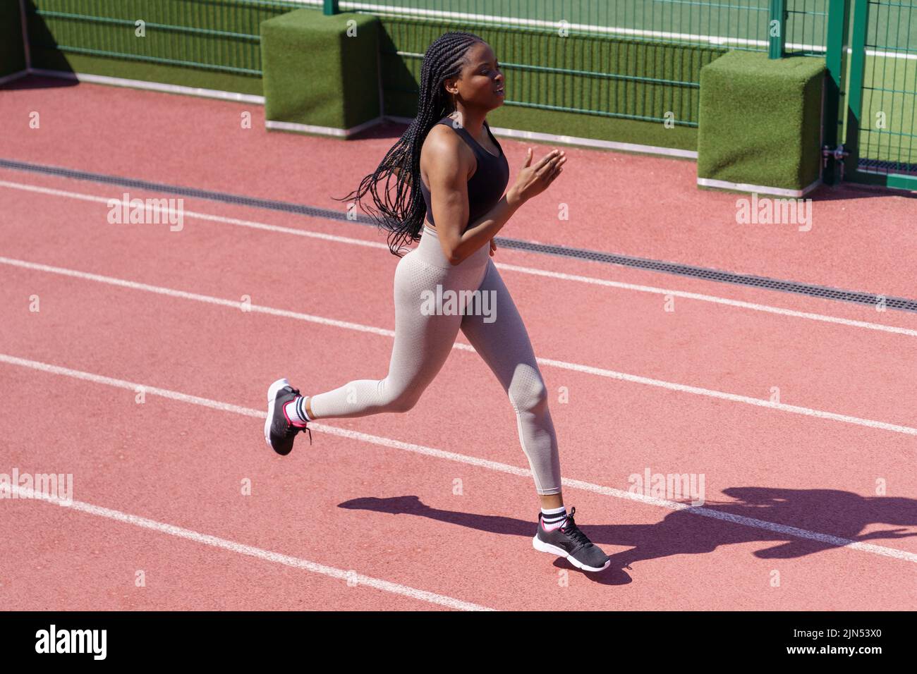 Sportive African American woman runs on red track around stadium to ...