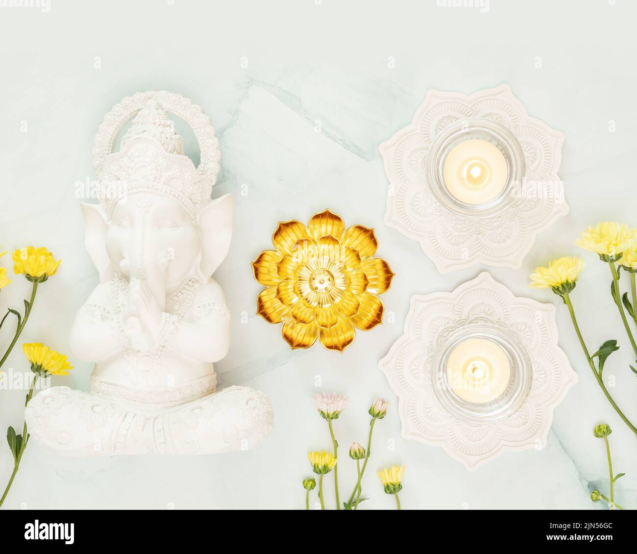 Sculpture of Lord Ganesha with flowers and candles on a light blue ...