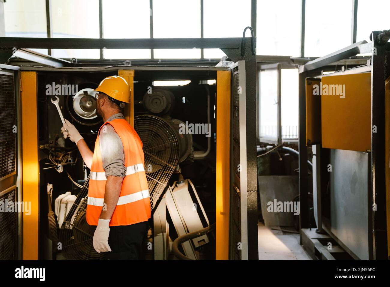 White ginger man wearing helmet and vest fixing equipment at factory ...