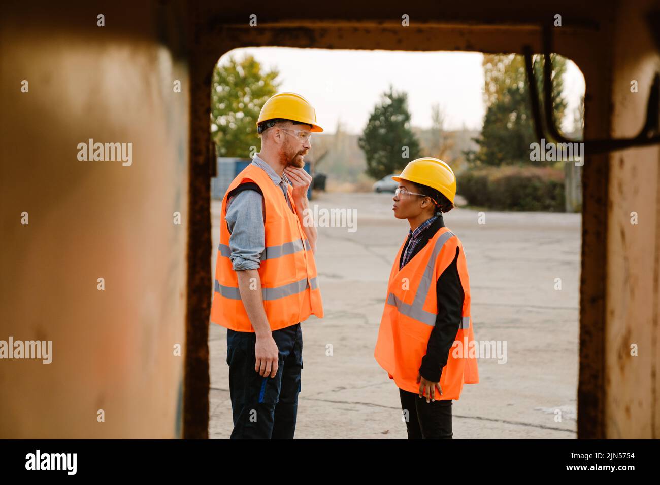 Multiracial man and woman wearing helmets talking while working ...