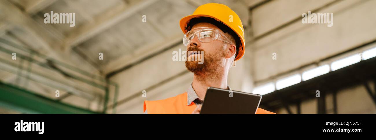 White man wearing helmet and vest using tablet computer while working ...