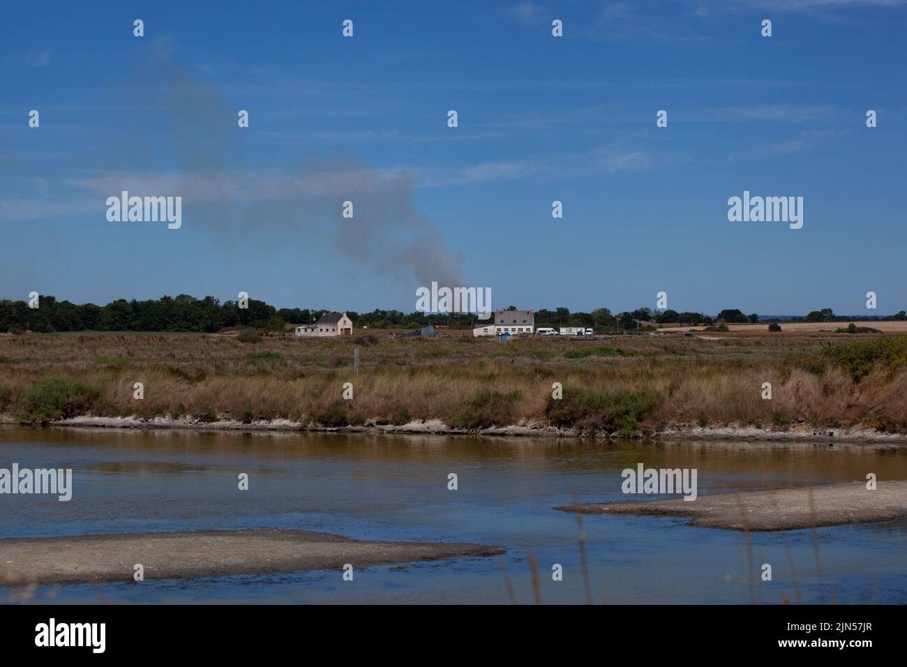 Black fire smoke rises in the sky above a marsh during the period of ...