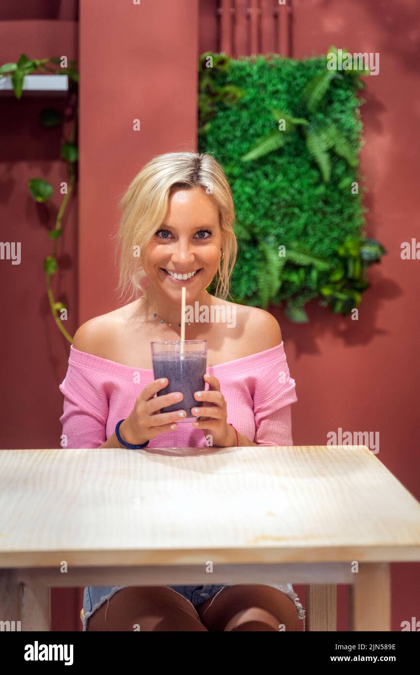 Happy woman smiling at camera while drinking a delicious smoothie in a ...