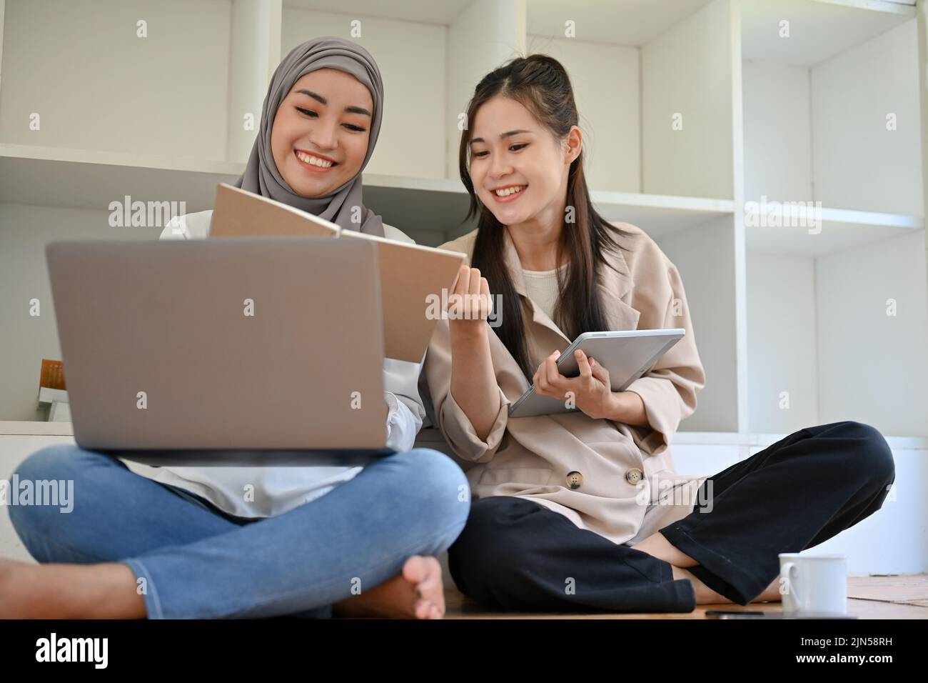 Beautiful young Asian female college student in the library co-working space with her Muslim ...