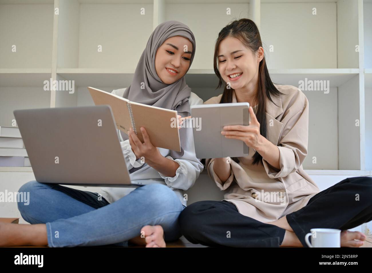 Attractive young Asian female college student in the library co-working space with her Muslim ...