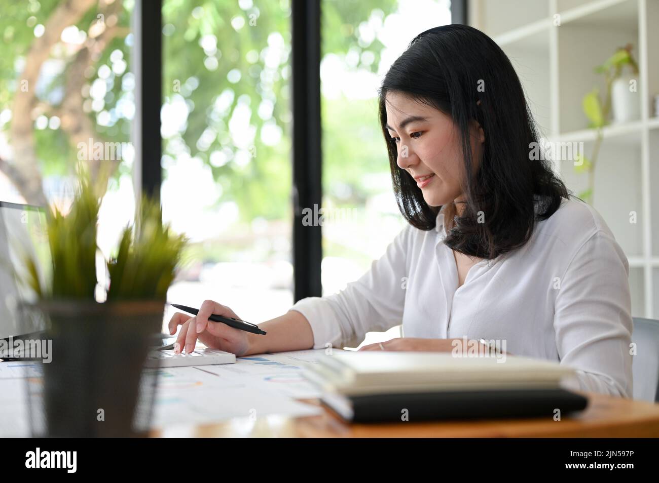 Attractive Asian female millennial accountant concentrating while ...