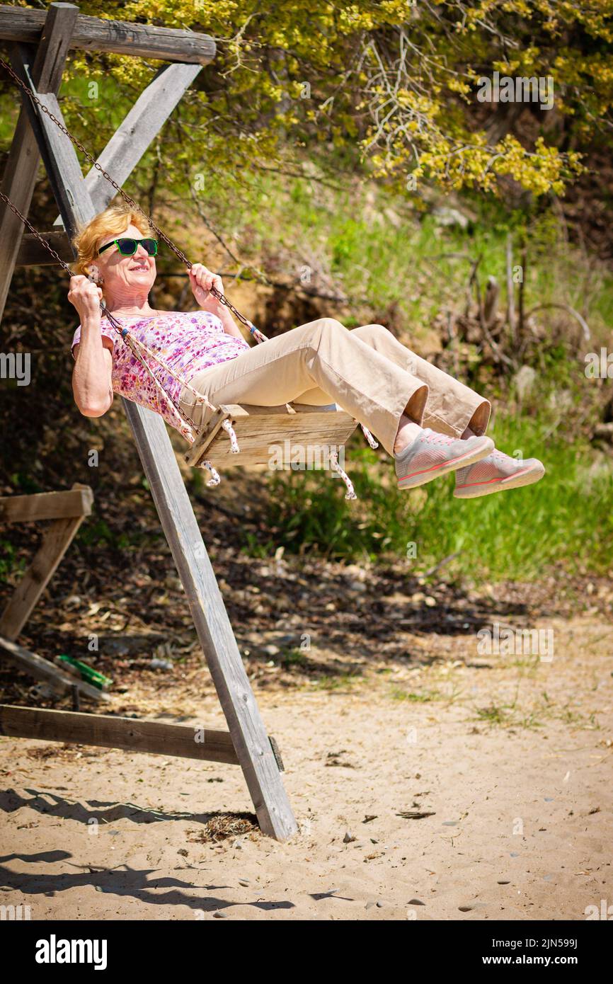 Senior woman joyfully swinging on a swing and having fan Stock Photo ...