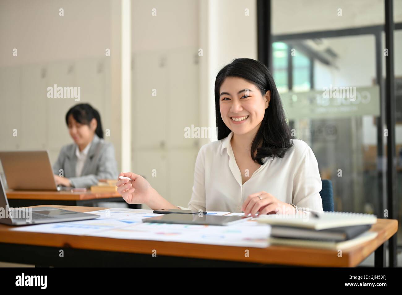 Charming and attractive young Asian female employee sits at her office ...