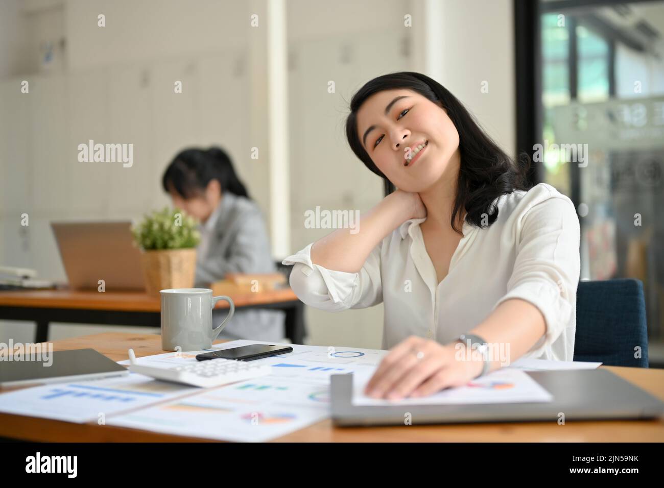 Tired and exhausted young Asian female office worker at her office desk ...