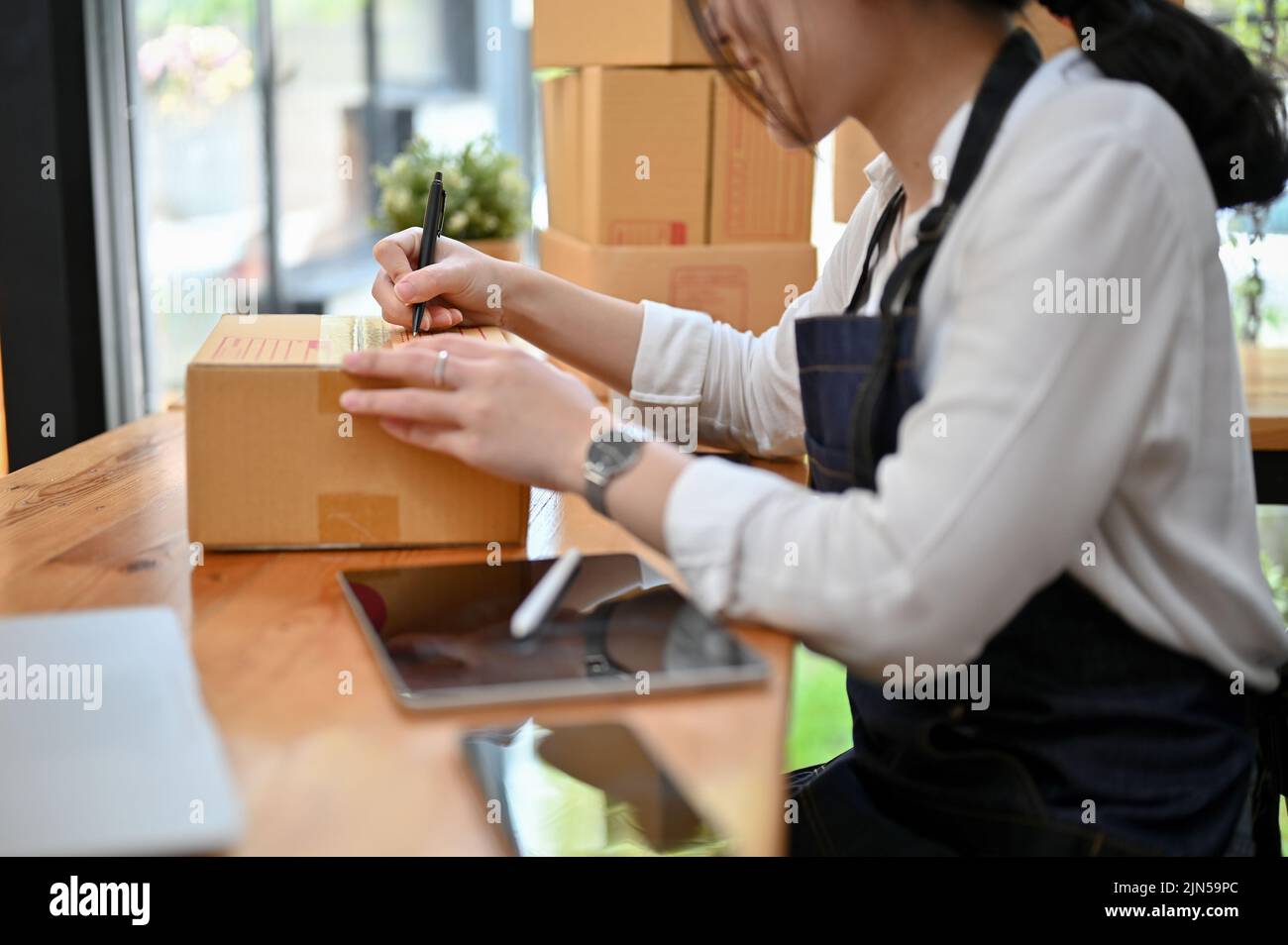 Pretty young Asian female e-commerce startup entrepreneur preparing her shipping packages in the ...