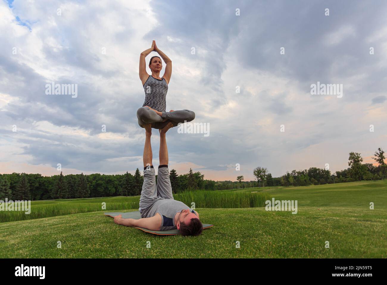 Young couple doing acro yoga in park. Man lying on grass and balancing ...