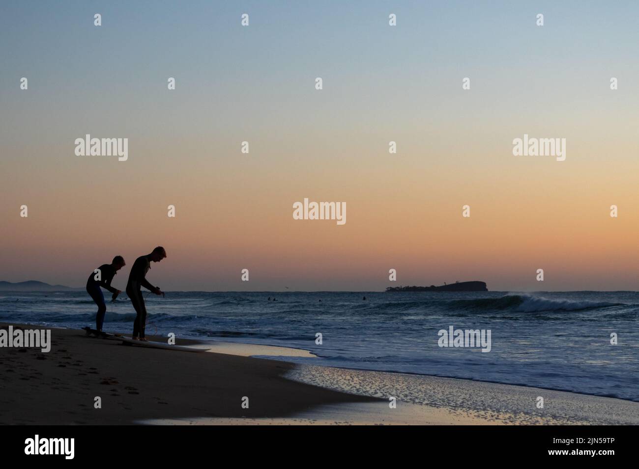 The silhouettes of two surfers on the shore getting ready to go to sea ...