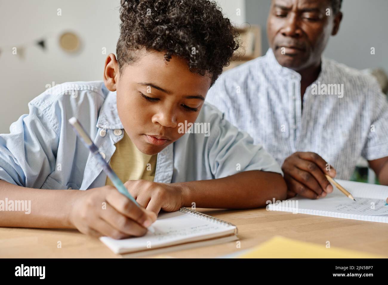African little boy making notes in his notebook at table and doing ...