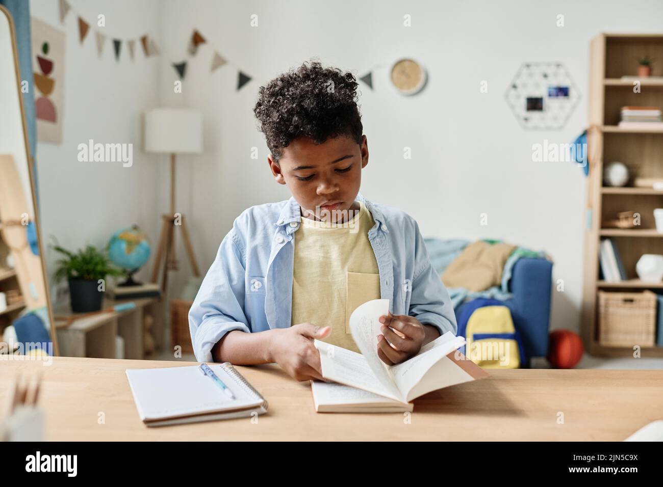 African little boy turning the pages of his book at the table while ...