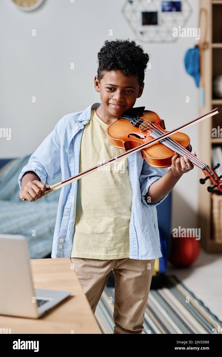 African boy looking at monitor on laptop on table and playing musical ...