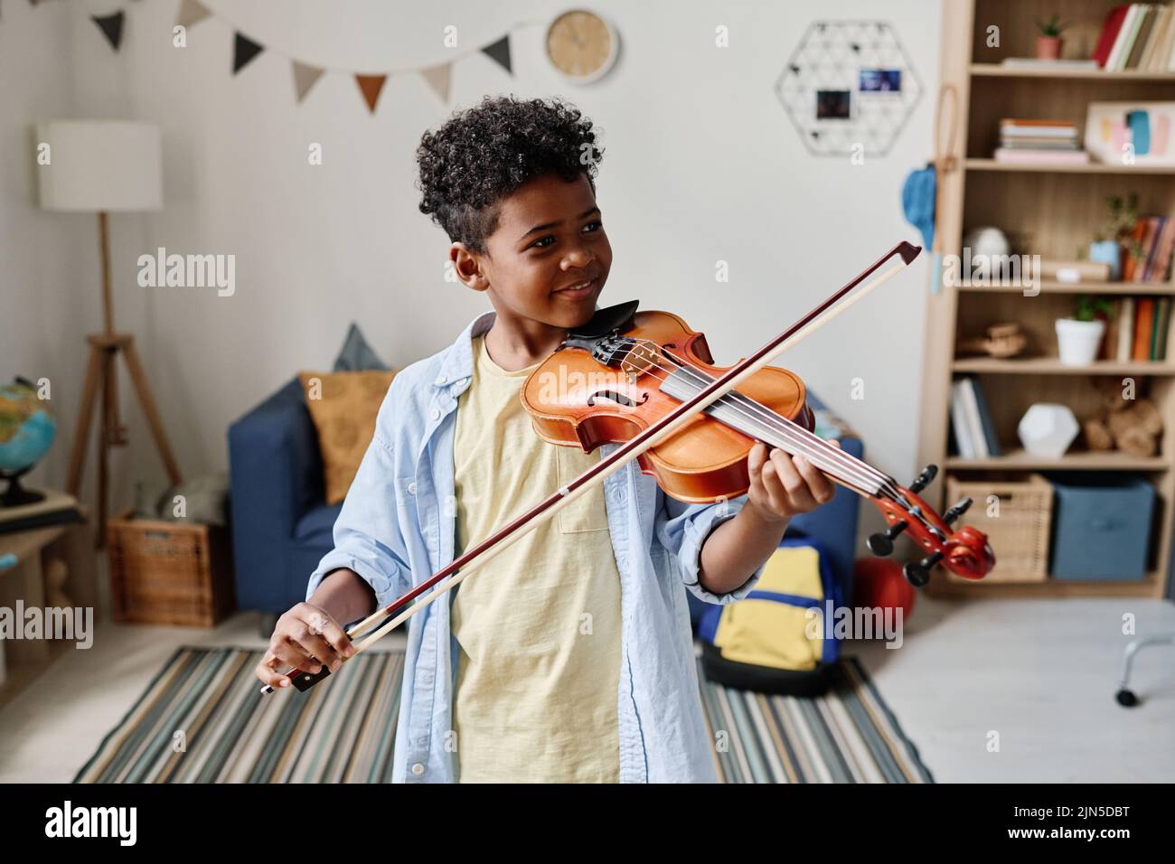 African boy playing violin during lesson while standing in his room at ...