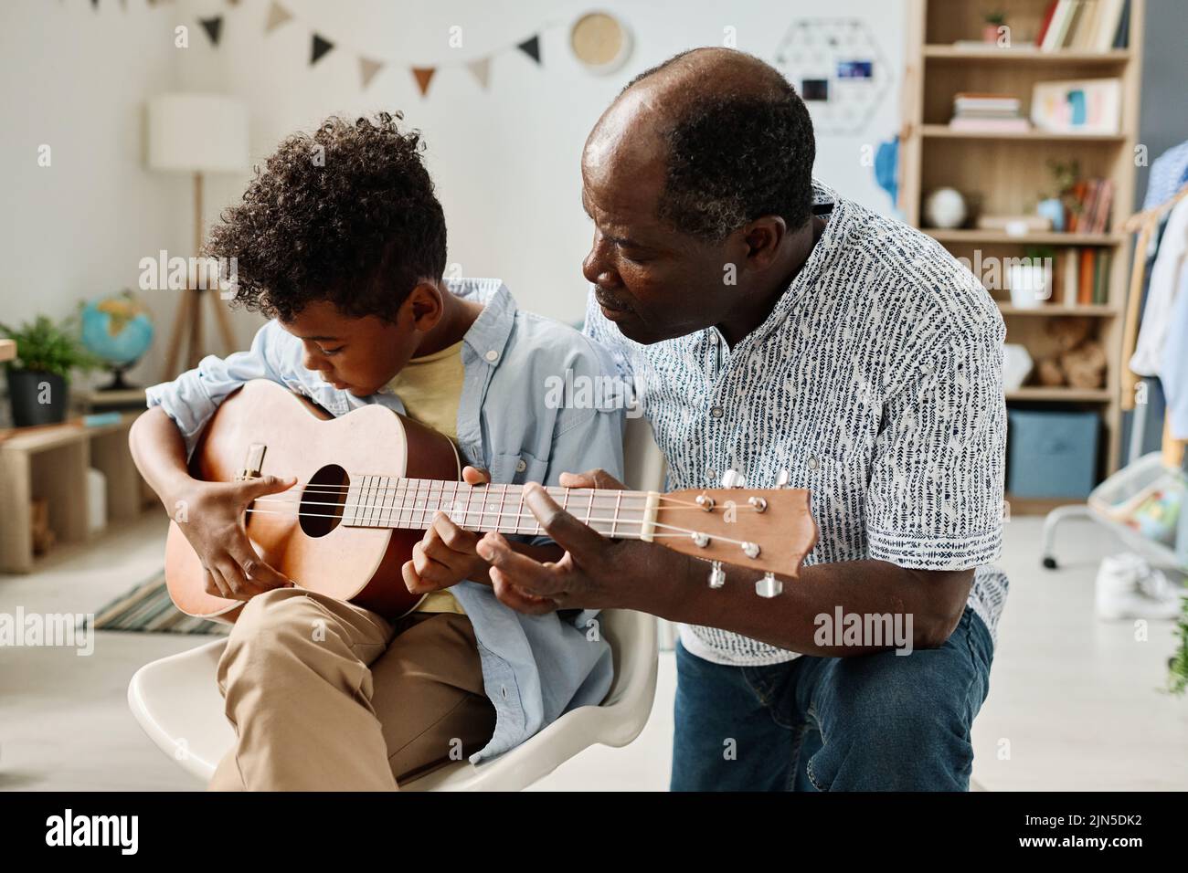 African boy having musical lesson with teacher at home, he teaching him ...