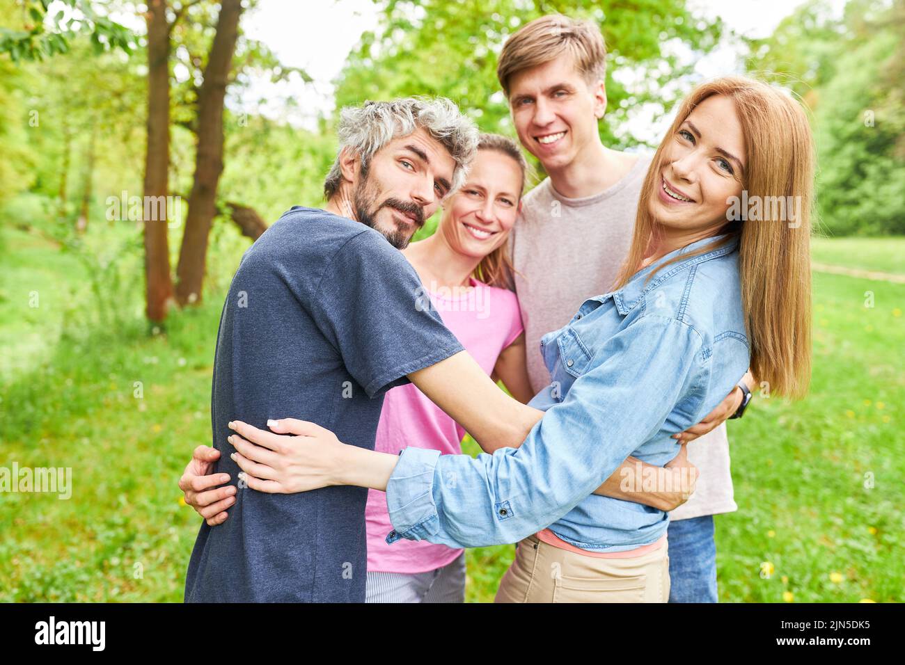 Group of young people hugging on a meadow in nature for friendship and ...