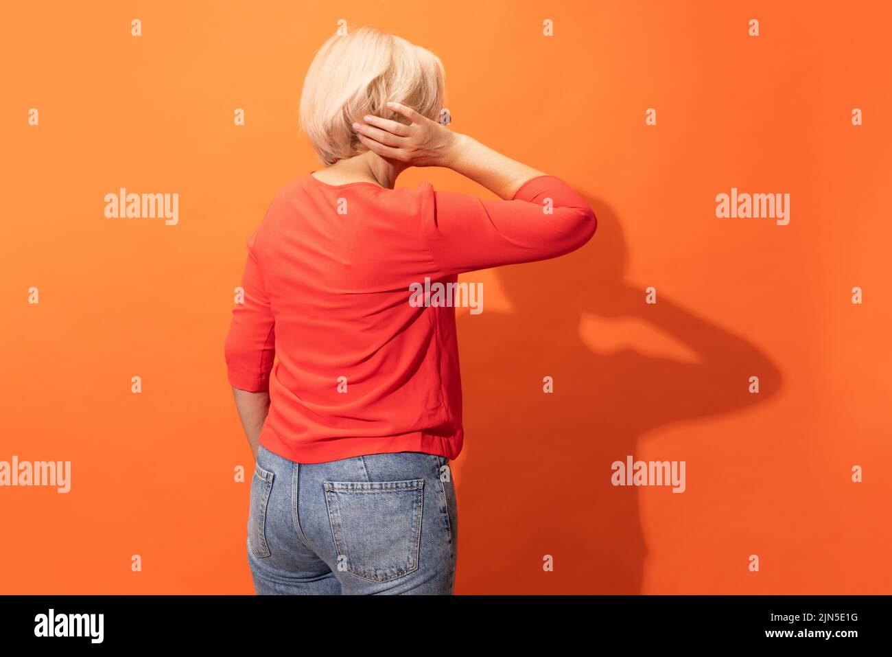 Back view of middle age woman with blond hair posing isolated on orange ...