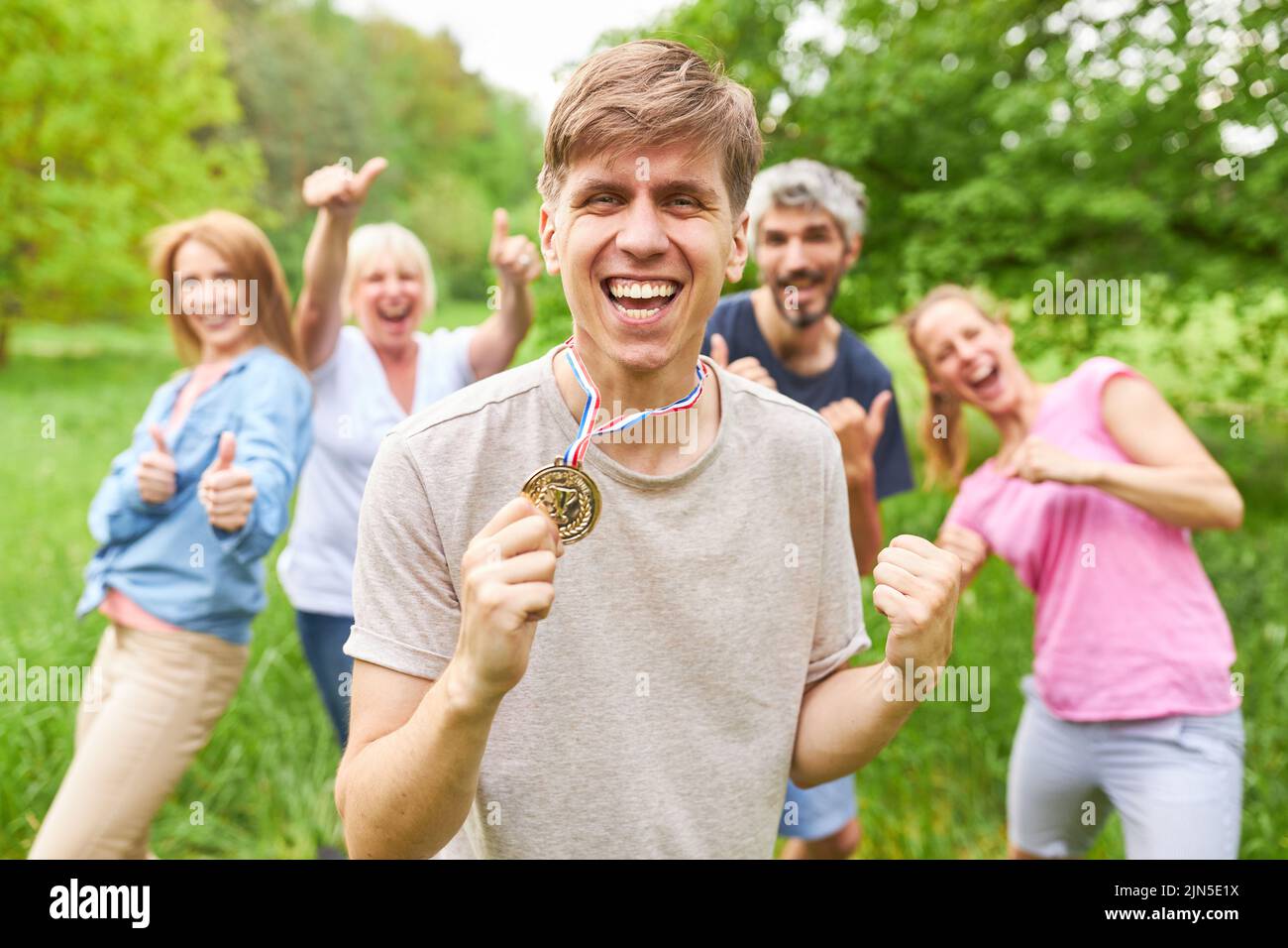 Happy man proudly shows his medal in front of cheering team after a win ...