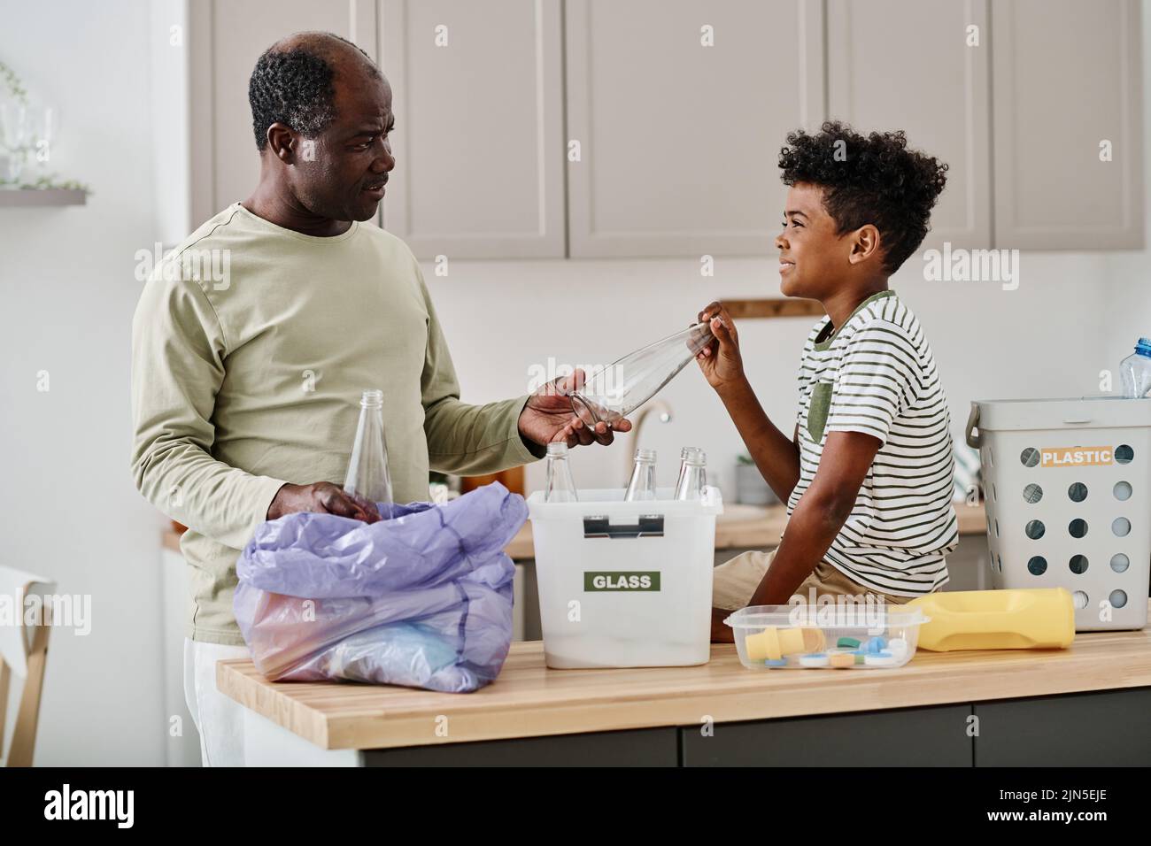 African dad giving glass bottles to his son to sort them in containers ...