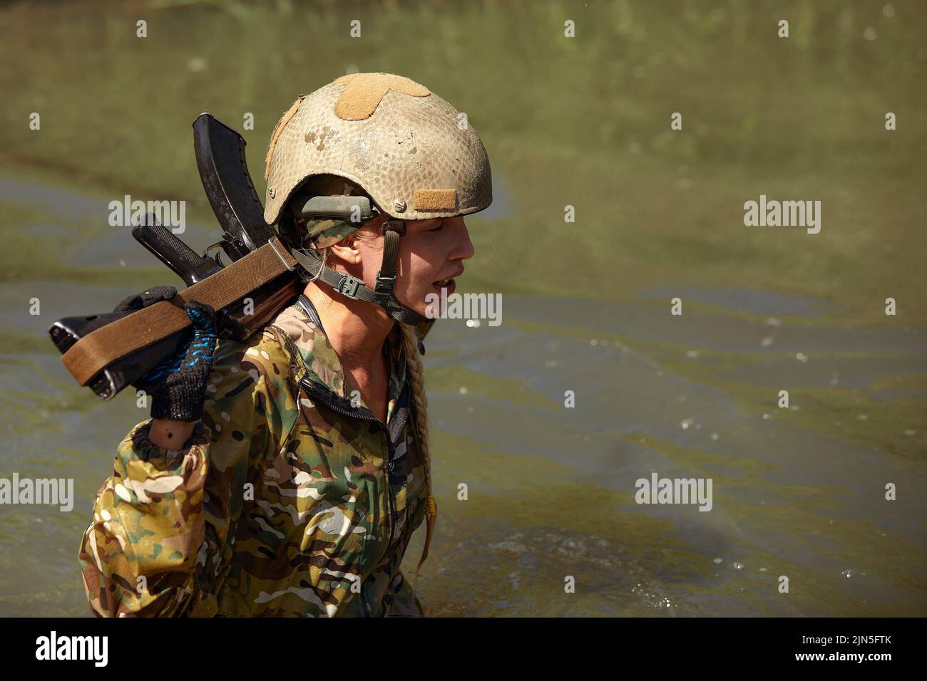 Portrait of fit military female holding weapon rifle in hands in river ...