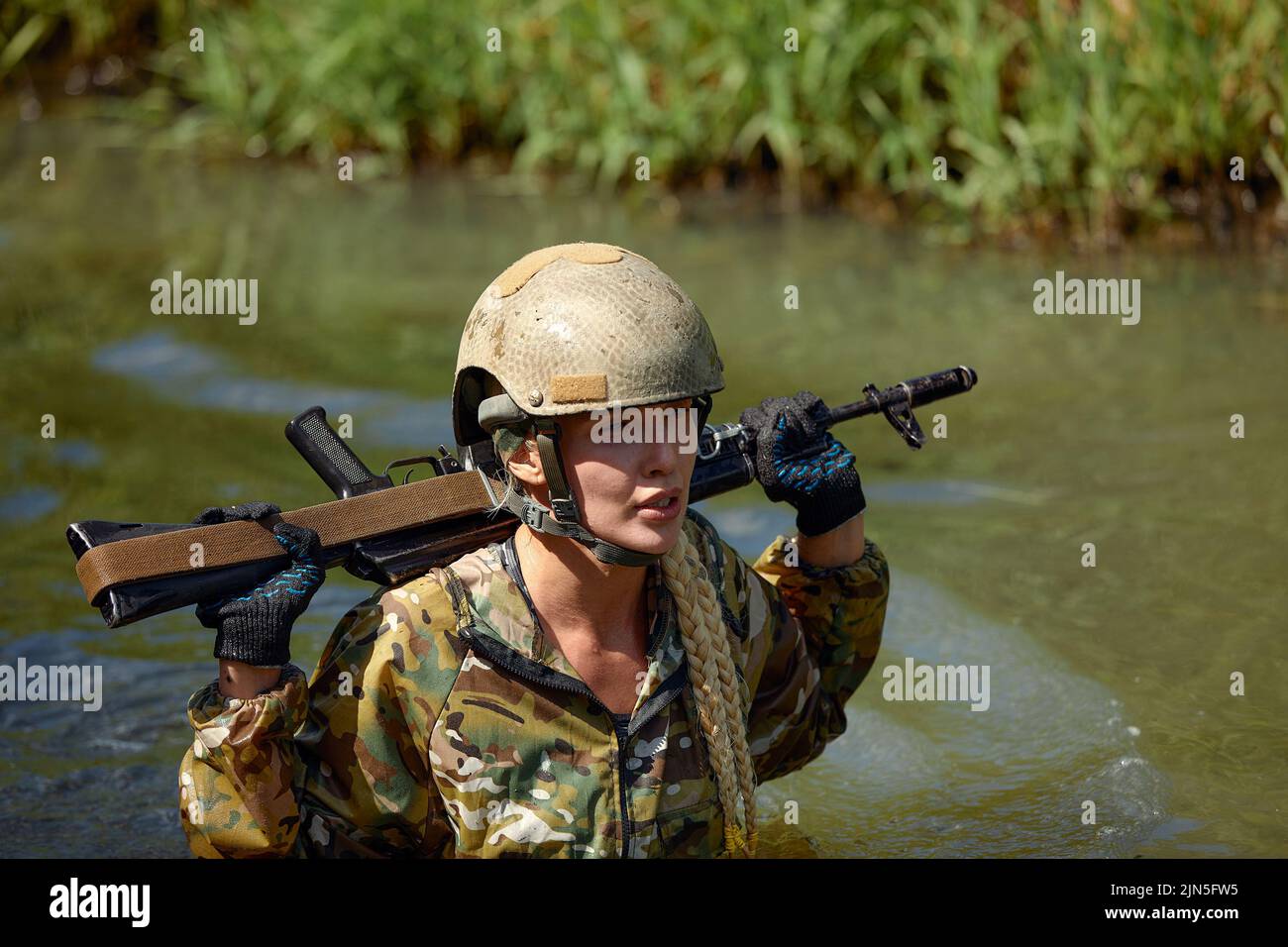 Portrait of fit military female holding weapon rifle in hands in river ...