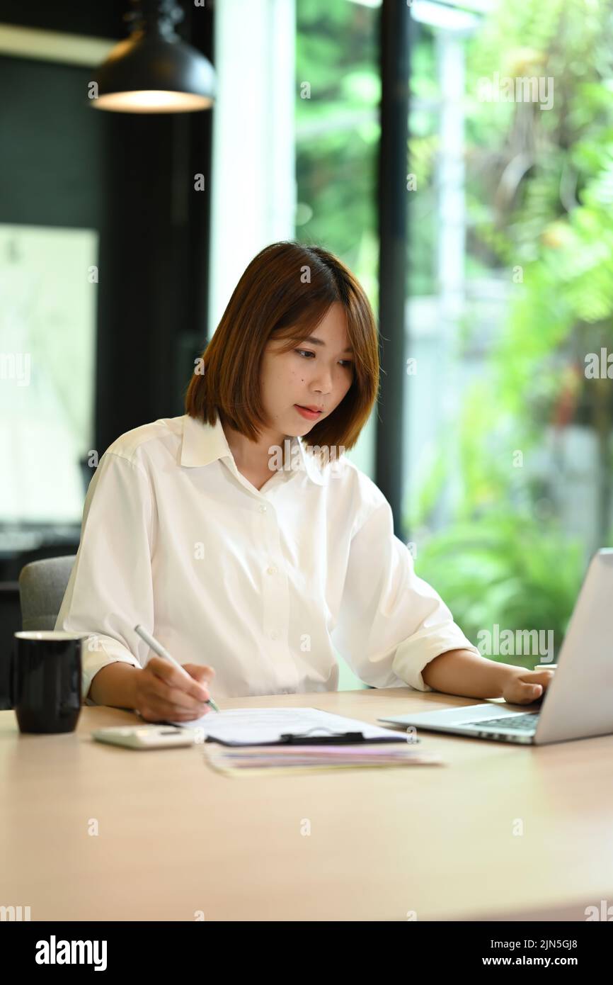 Concentrated female economist using laptop an working with document at ...