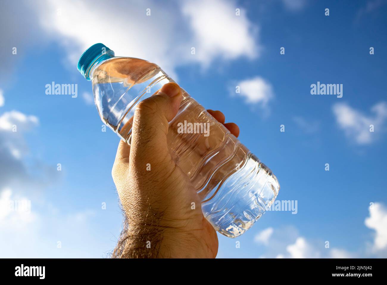 Water in plastic bottle outdoors under blue sky. hand holding water Stock Photo - Alamy