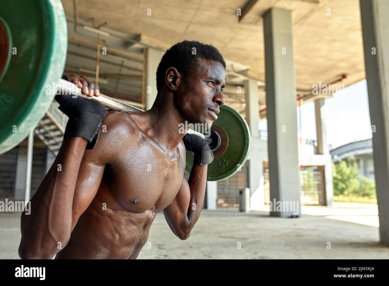 Athletic black young man lifting a heavy-weight barbell in outdoor gym ...