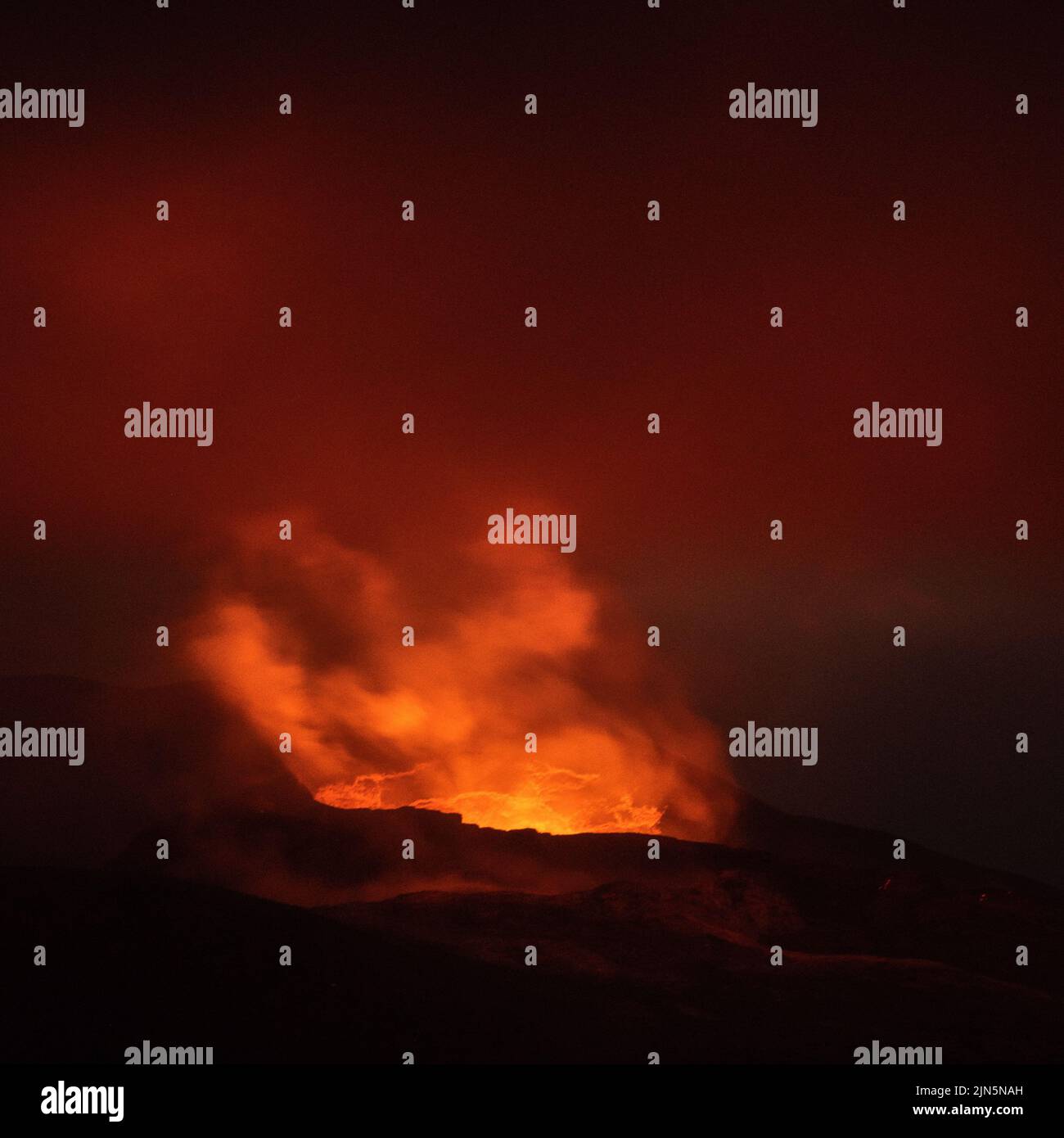 A beautiful shot of a volcano erupting at night with a red smoke cloud ...