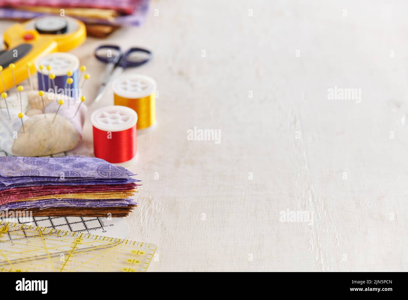 Ruler, cutting mat, stack of multi-colored pieces of fabric, pincushion ...