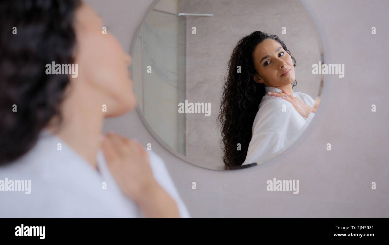 Young woman in bathrobe looks in mirror in bathroom attractive ...