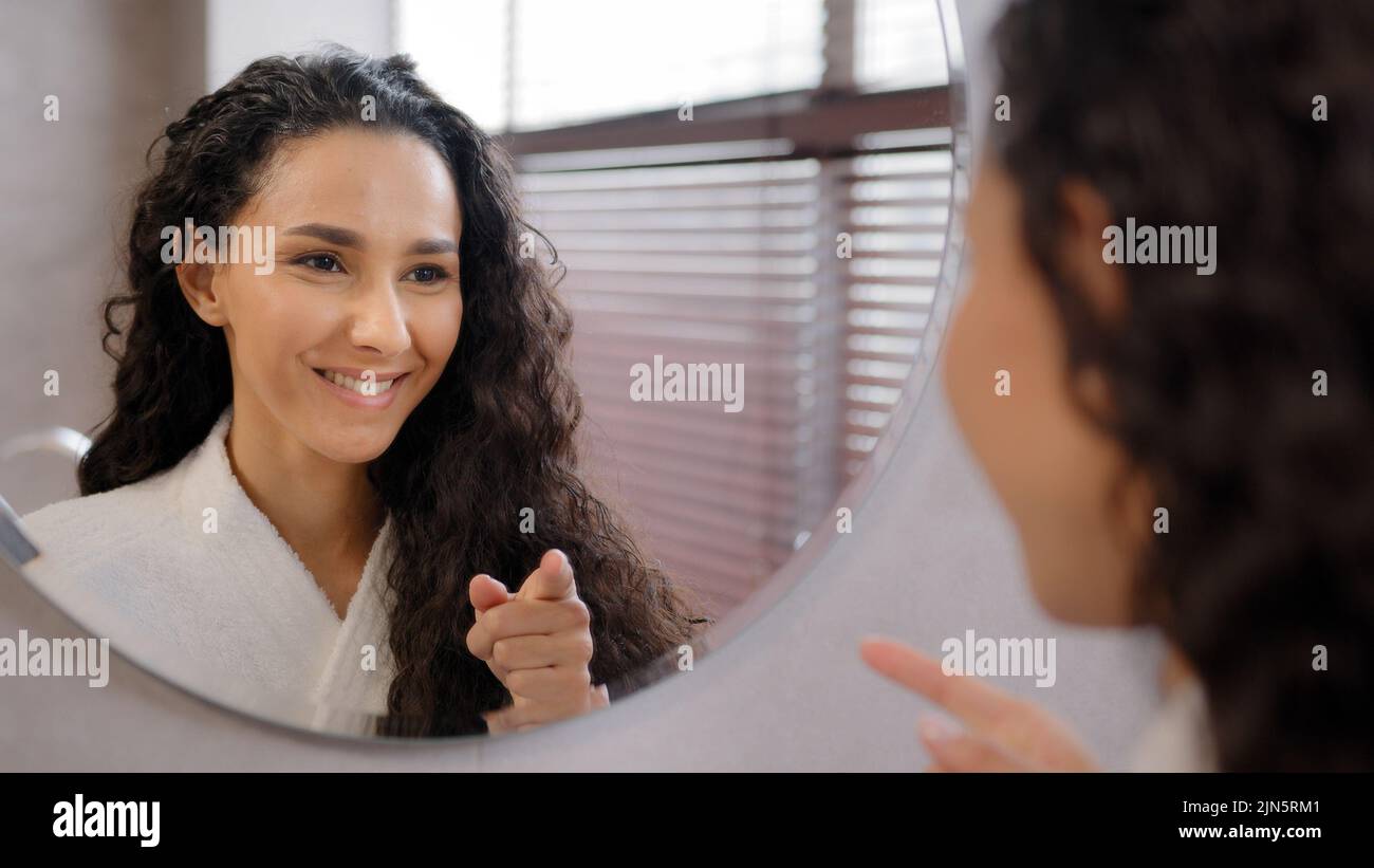 Young happy confident woman standing in bathroom looking in mirror ...