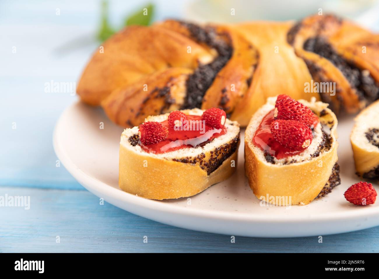 Homemade sweet bun with strawberry jam and cup of green tea on a blue ...