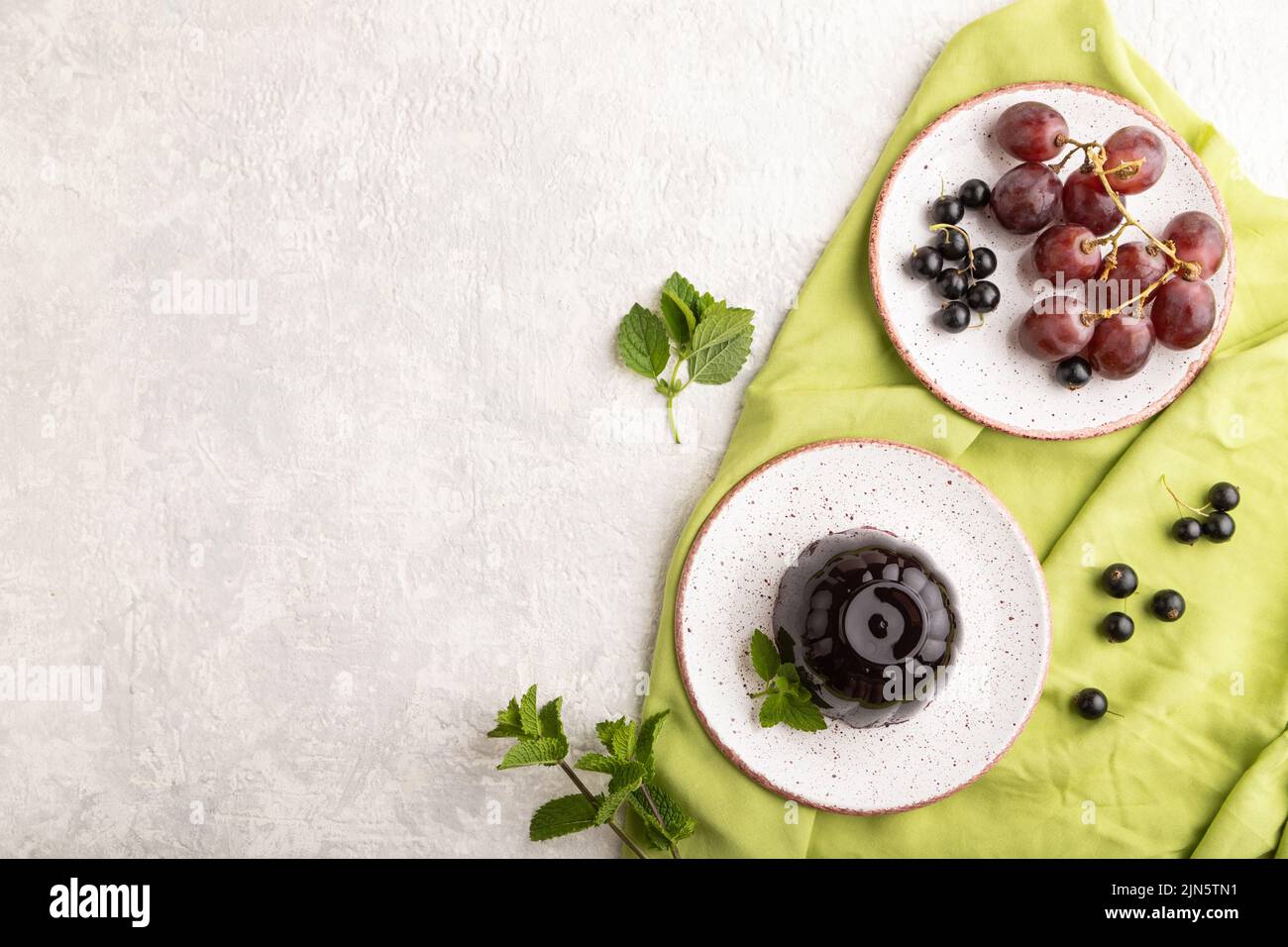 Black currant and grapes jelly on gray concrete background and green ...