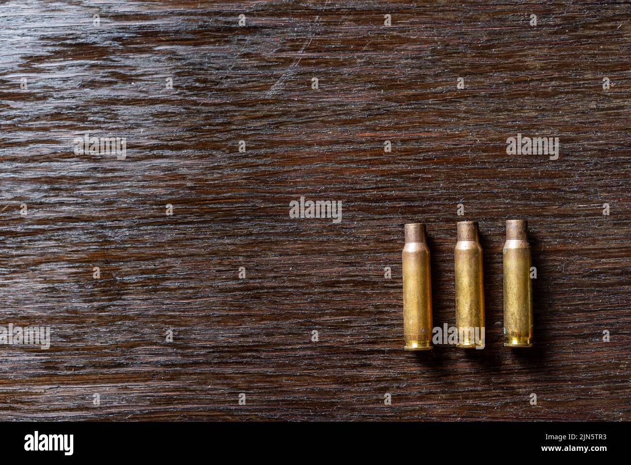 A close-up shot of three empty bullet casings on a dark, wooden table ...